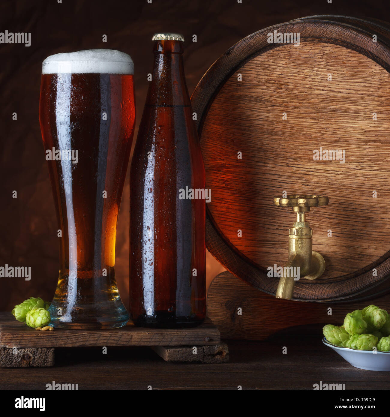 Bottled and unbottled beer glass with barrel and fresh hops for brewing ...