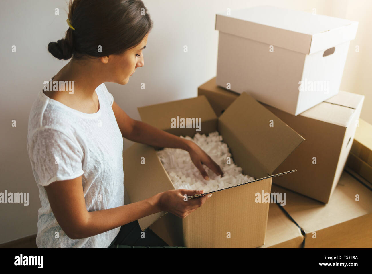Woman unpacking moving boxes into new apartment. Side view of woman ...