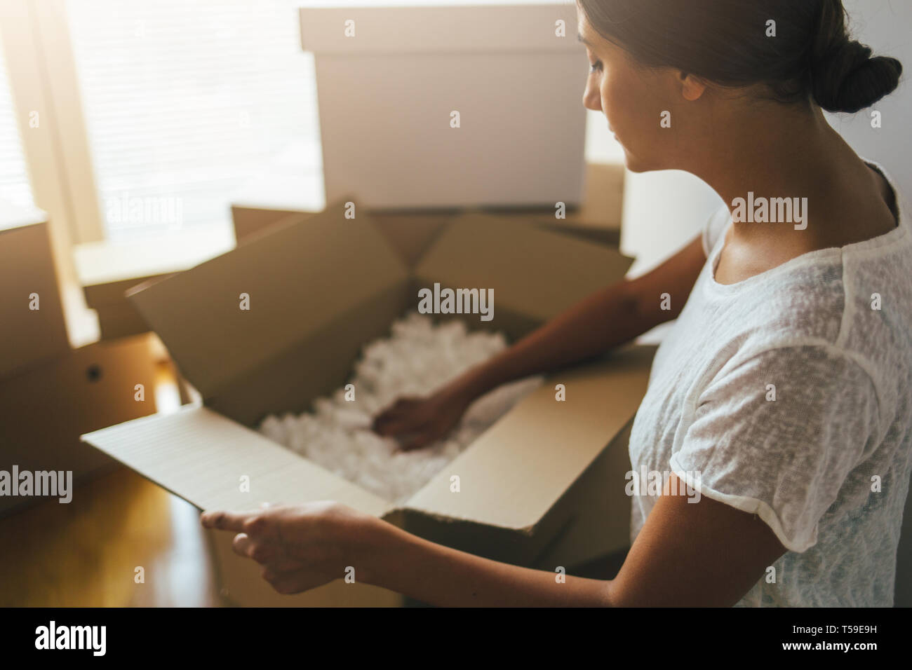 Woman unpacking moving boxes into new apartment. Side view of woman ...