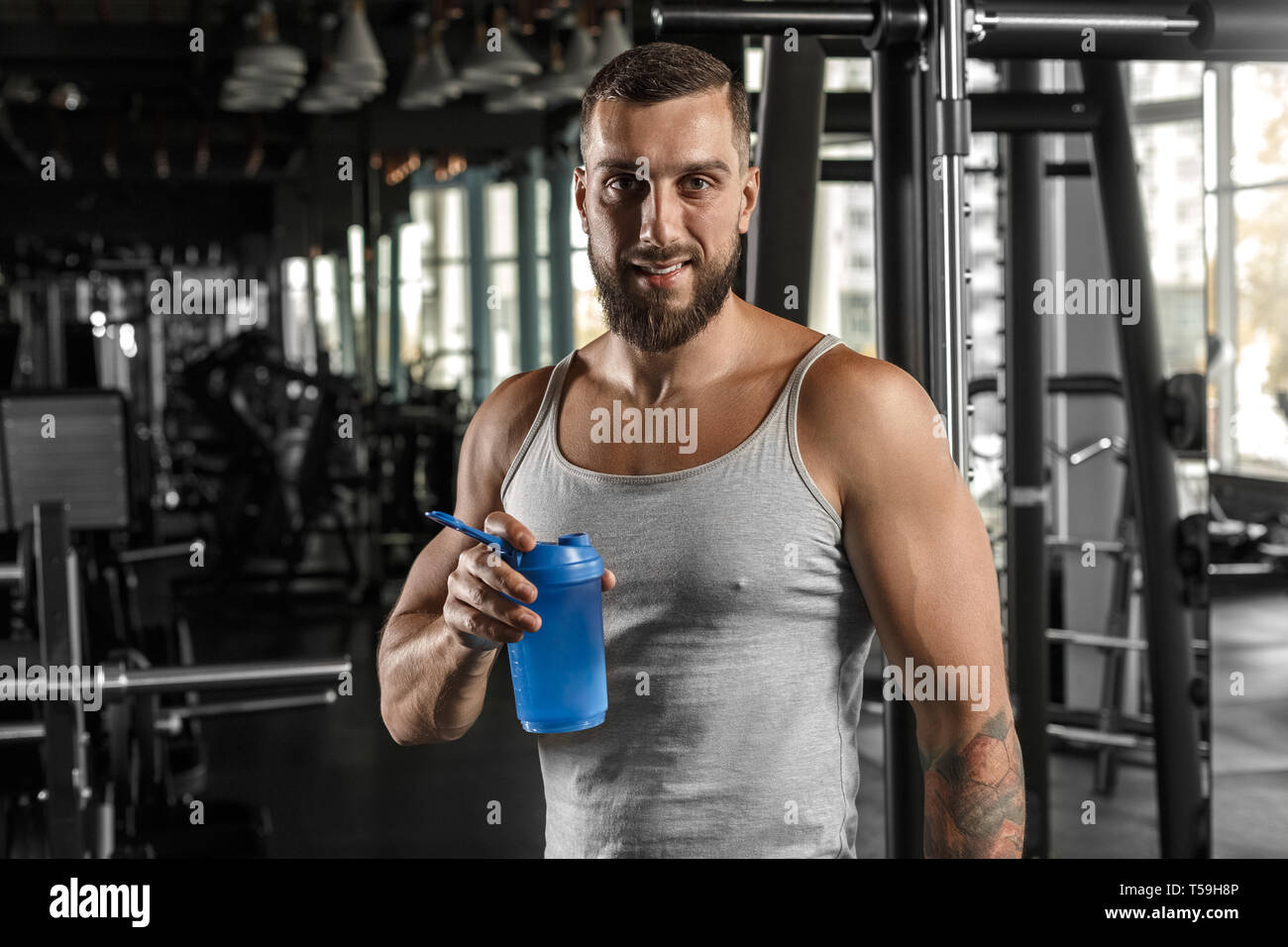 Bodybuilding. Bearded man standing at gym with bottle drinking protein ...