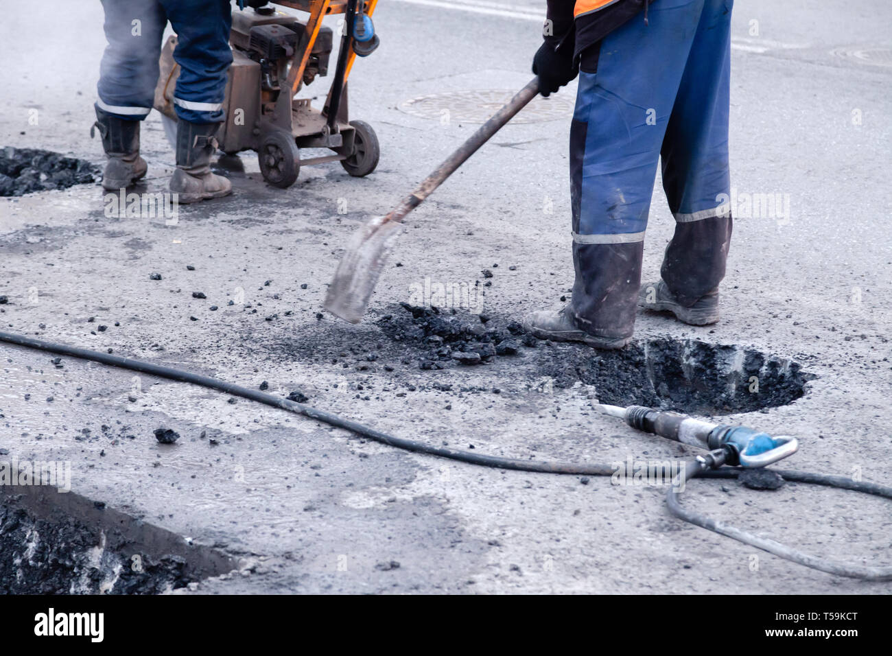 Professional workers in uniforms repair the road, cut off the asphalt ...