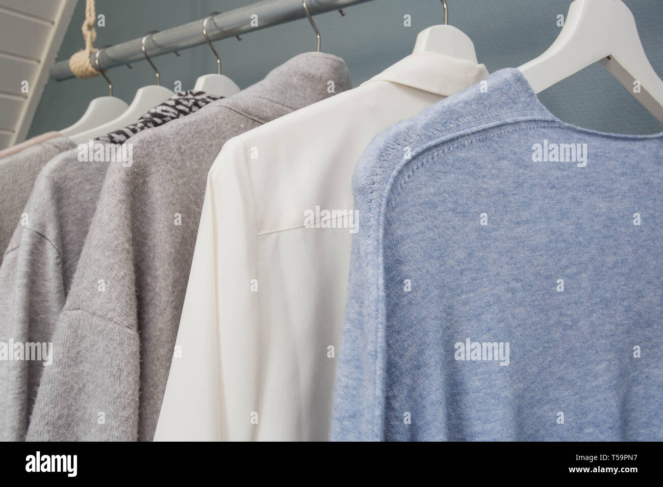 Clothes hang on a a clothing rack, white gray and blue Stock Photo - Alamy