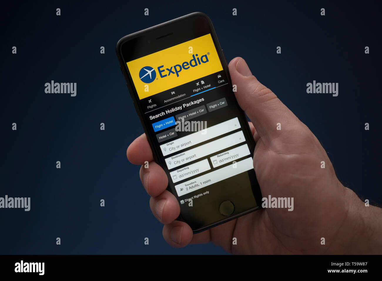 A man looks at his iPhone which displays the Expedia logo (Editorial ...