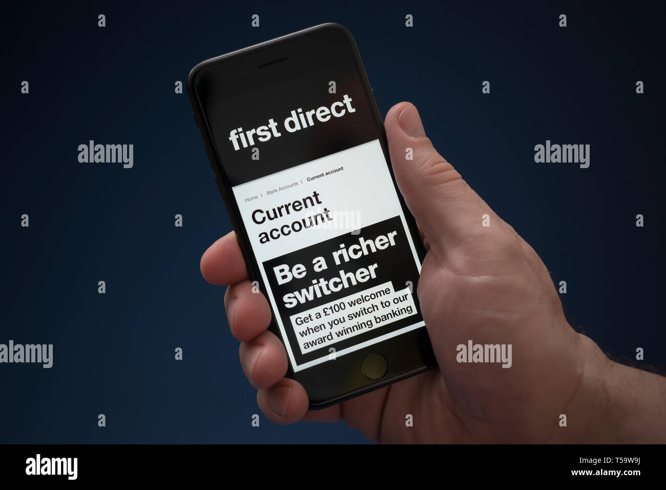 A man looks at his iPhone which displays the First Direct logo ...
