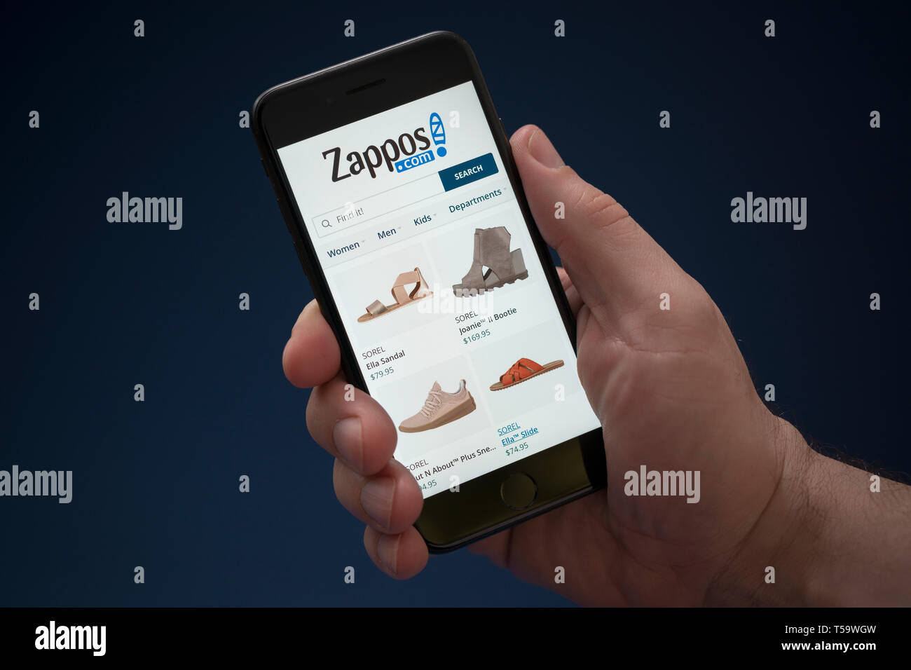 A man looks at his iPhone which displays the Zappos logo (Editorial use ...