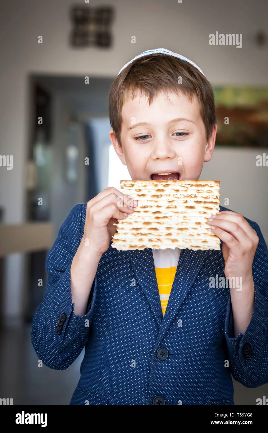 Cute Caucasian child in a yarmulke taking a bite from a traditional ...