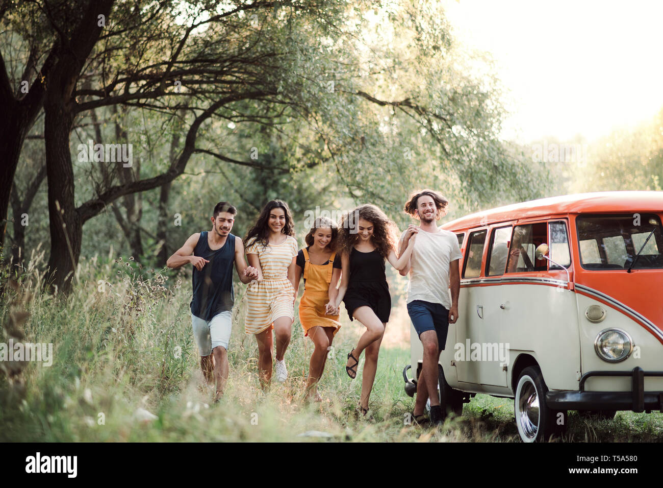 A group of young friends walking by a retro minivan on a roadtrip ...