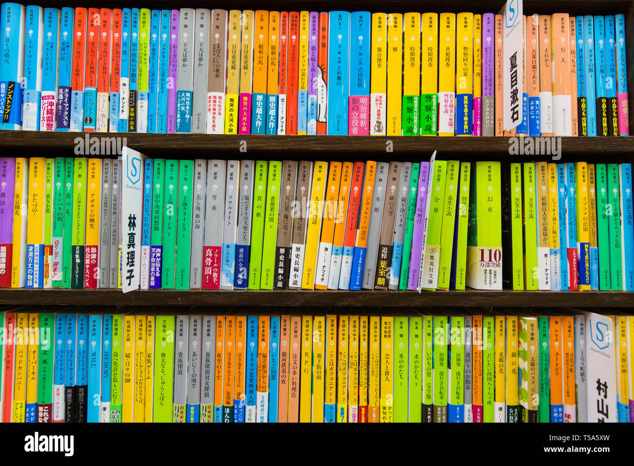 Three rows of japanese books neatly arranged on the shelf in a bookshop ...