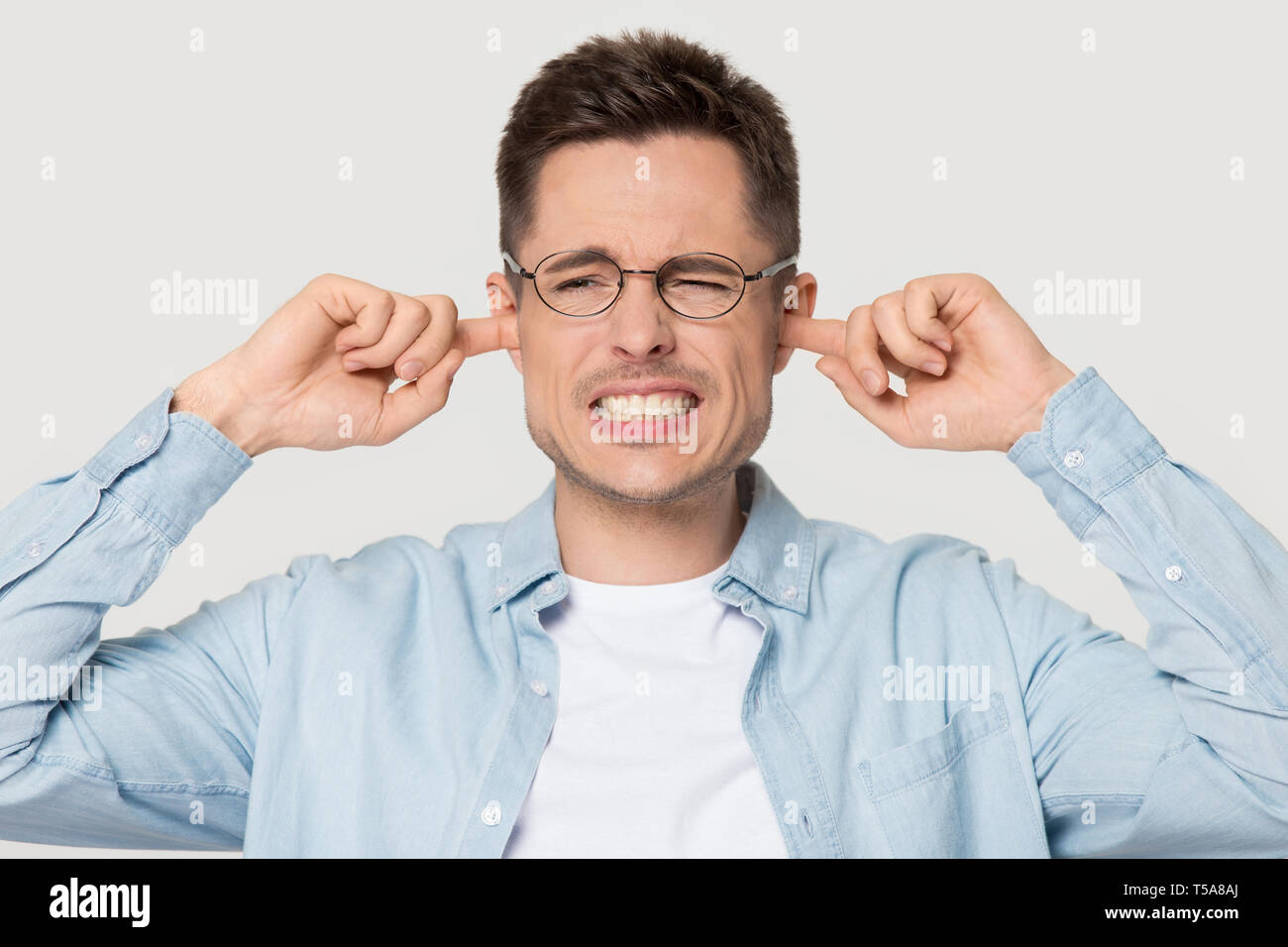 Annoyed man in glasses cover ears avoiding loud sound Stock Photo - Alamy