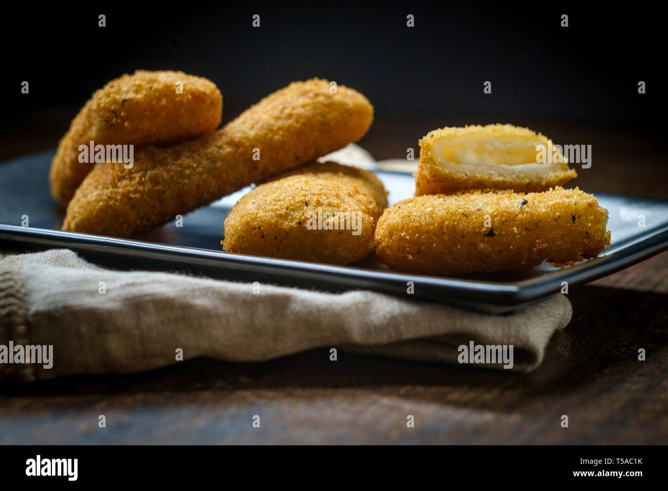 Breaded fried mozzarella cheese sticks on wooden kitchen table with ...