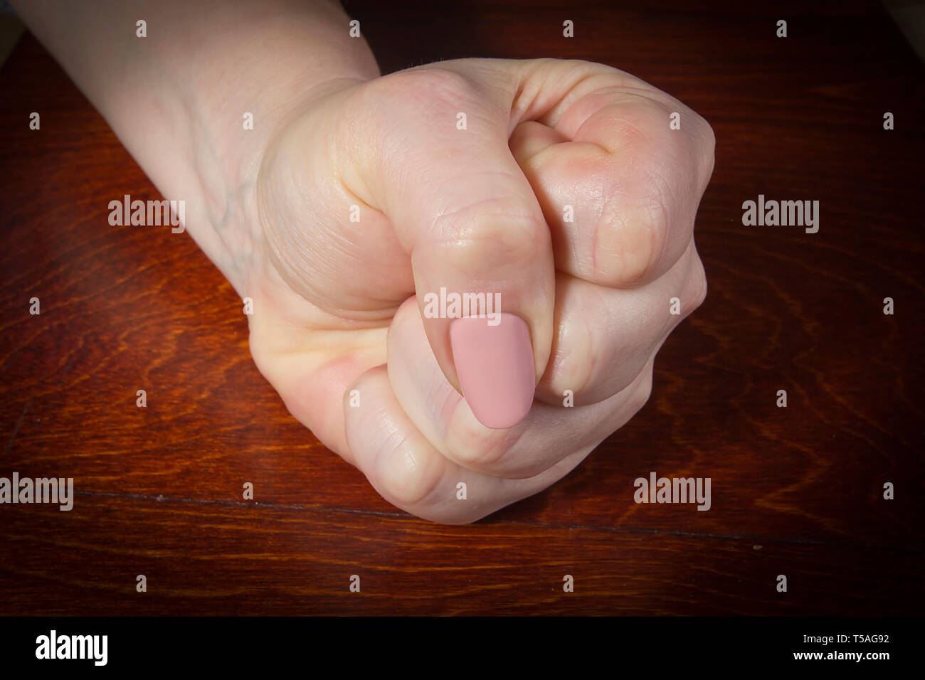 Female hand clenched into a fist on a wooden table Stock Photo - Alamy