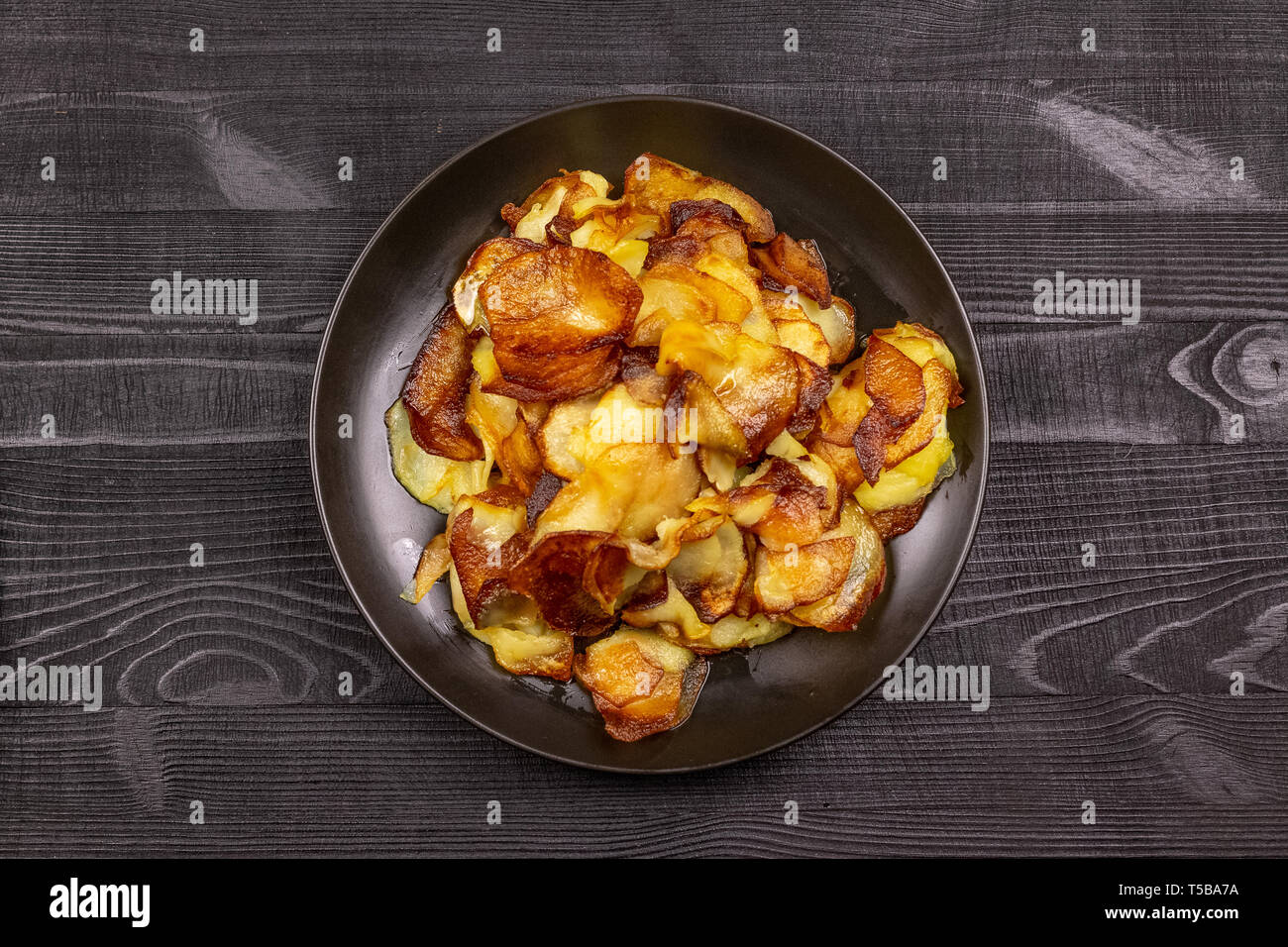Fried homemade potato chips in a black plate on a wooden rustic ...