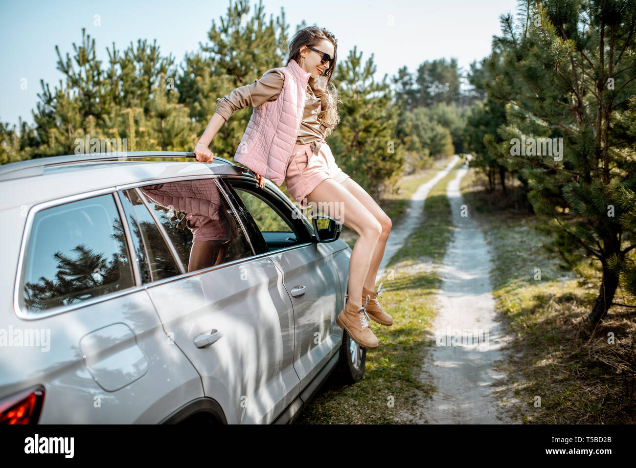 Woman jumping from the car roof while traveling by car in the forest ...