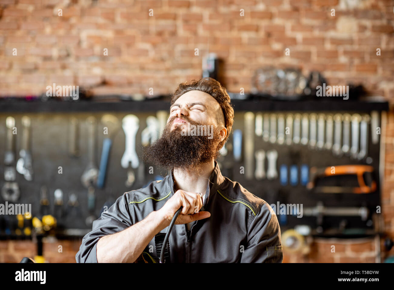 Funny repairman blowing with air pump on his beard at the bicycle ...