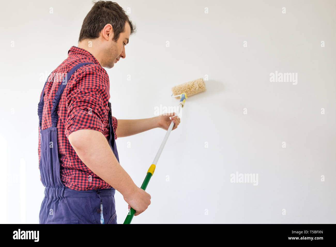 One standing painter man at work with a roller painting a white wall ...