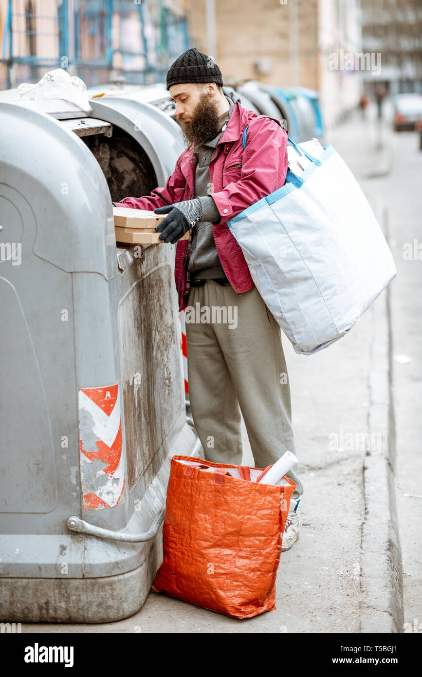 Homeless bearded beggar searching some food, rummaging in the trash in ...