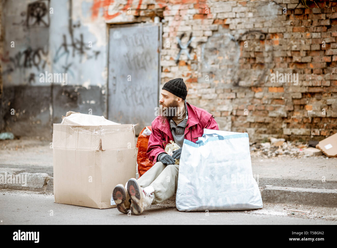 Homeless depressed beggar sitting with bags and cardboards on the ...