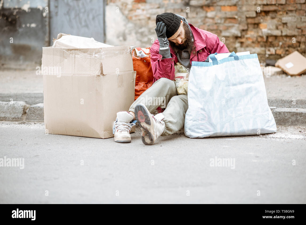 Homeless depressed beggar sitting with bags and cardboards on the ...