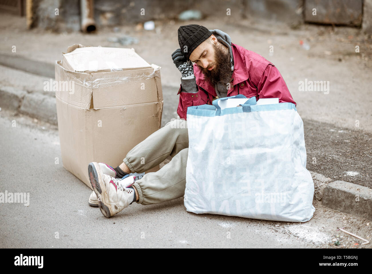 Homeless depressed beggar sitting with bags and cardboards on the ...