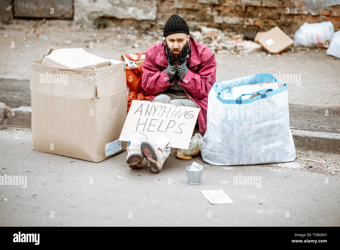 Homeless depressed beggar sitting with bags and cardboards on the ...