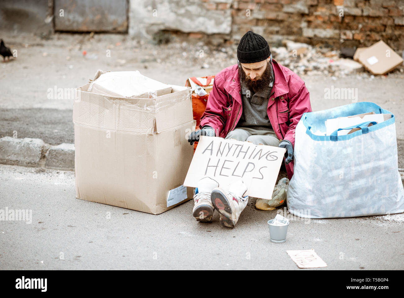 Homeless depressed beggar sitting with bags and cardboards on the ...