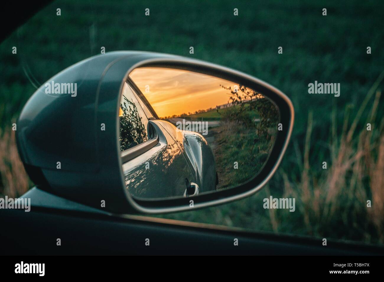 Beautiful sunset in the sideview mirror of the car. Green nature ...