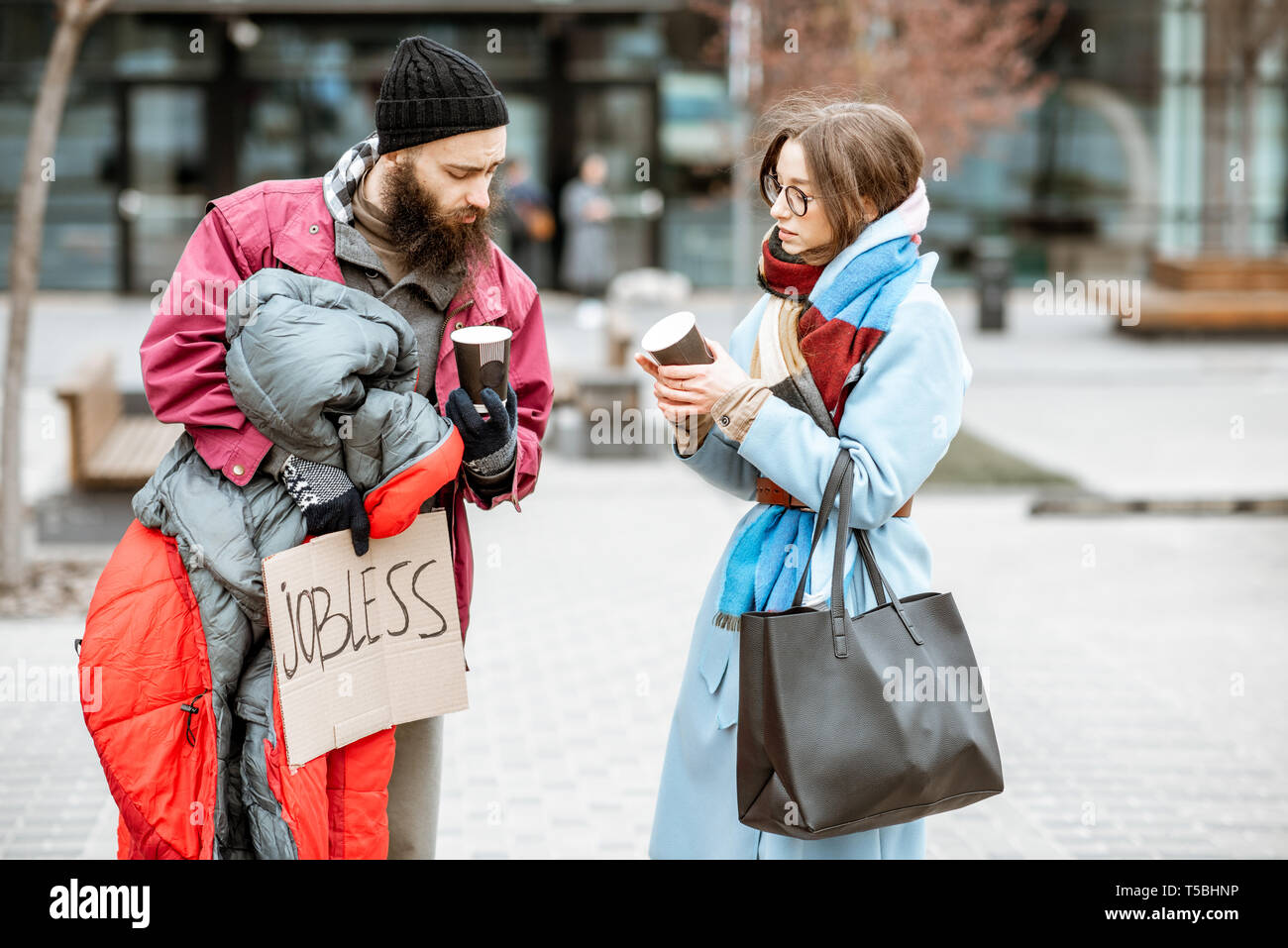 Homeless beggar talking with passing by woman while standing together ...