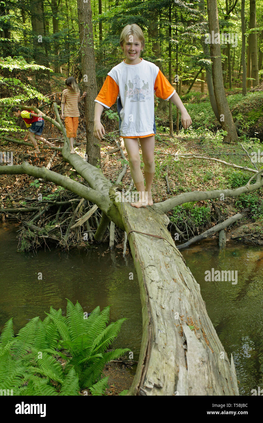 young boy walking barefoot over a tree trunk that is lying across a ...