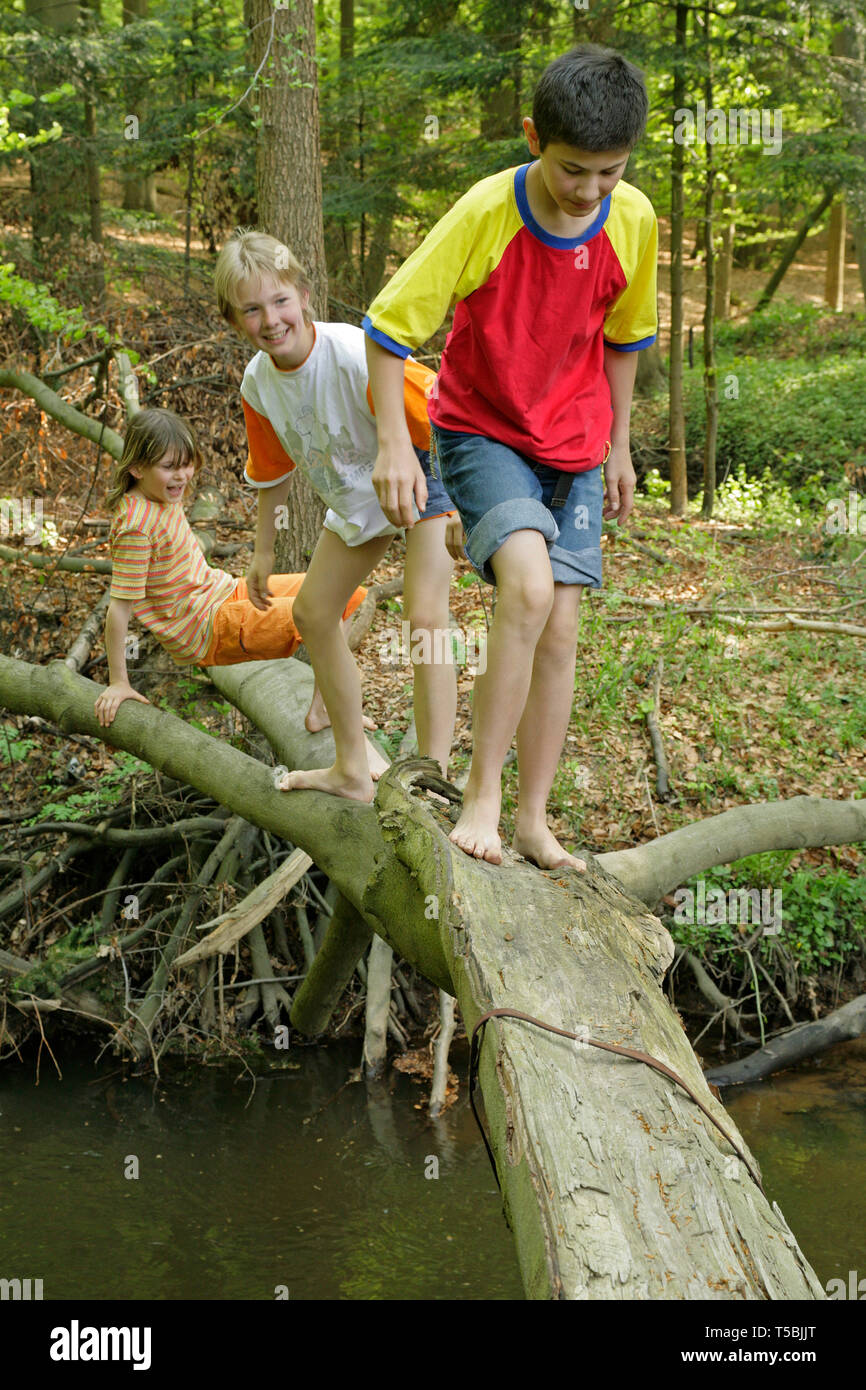 young boy walking barefoot over a tree trunk that is lying across a ...