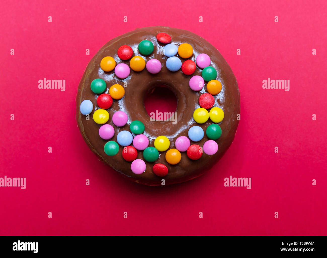Chocolate donut decorated with colorful smarties isolated on red color ...