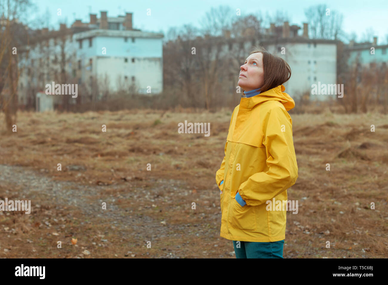 Woman in yellow raincoat looking up at rainy clouds while the raindrops ...