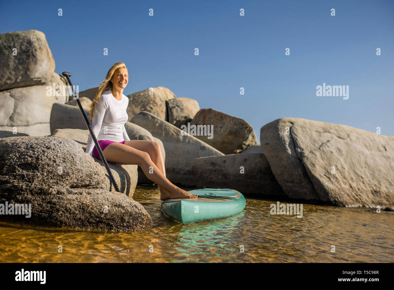 Paddle boarder sitting on a rock Stock Photo - Alamy