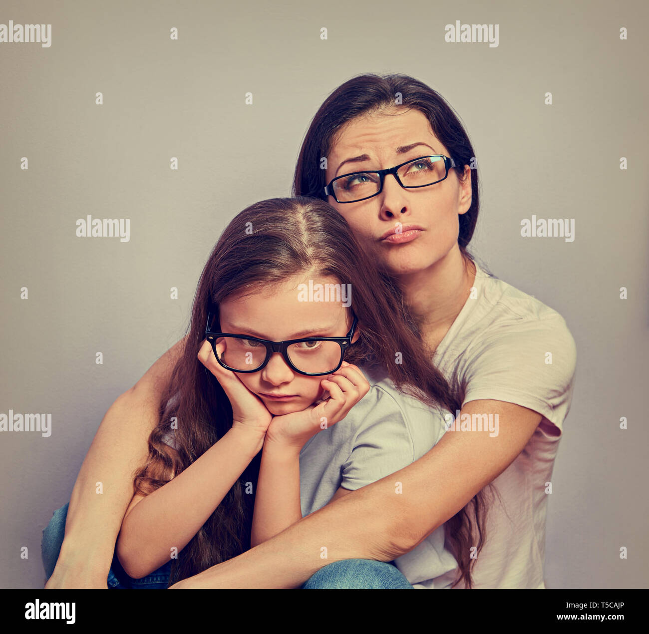 Sad young casual mother looking up and hugging her cute unhappy ...