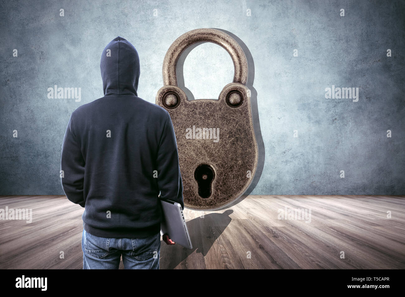 back view of a hacker in the hood with a laptop in hand, in an empty ...