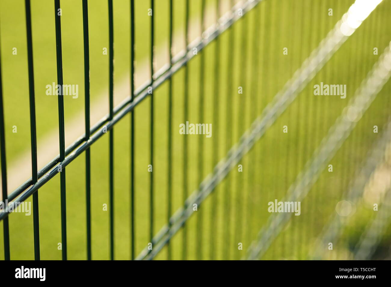 grid of green fence on the background of the lawn field for playing ...
