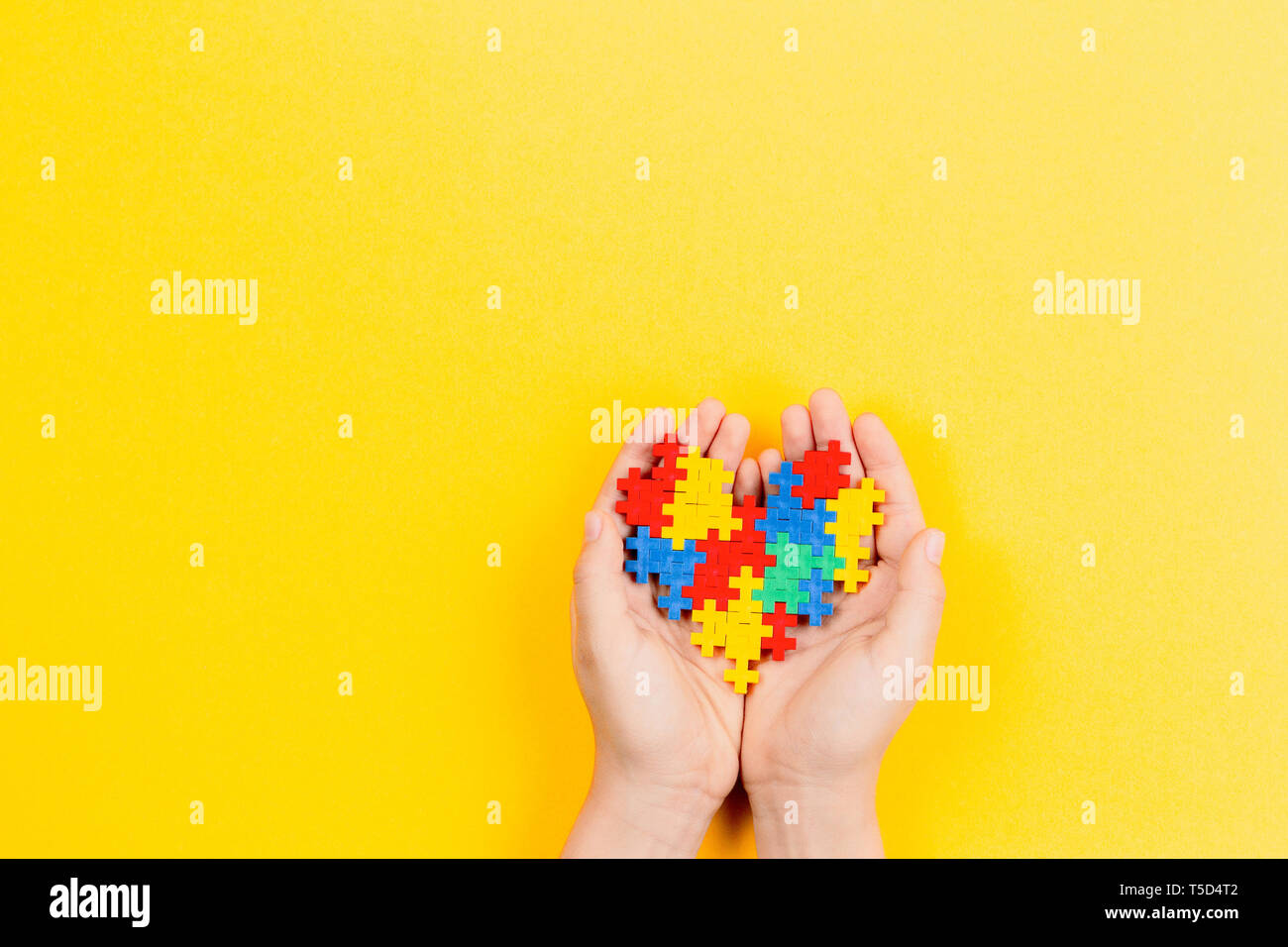 Child hand holding colorful heart on yellow background. World autism ...