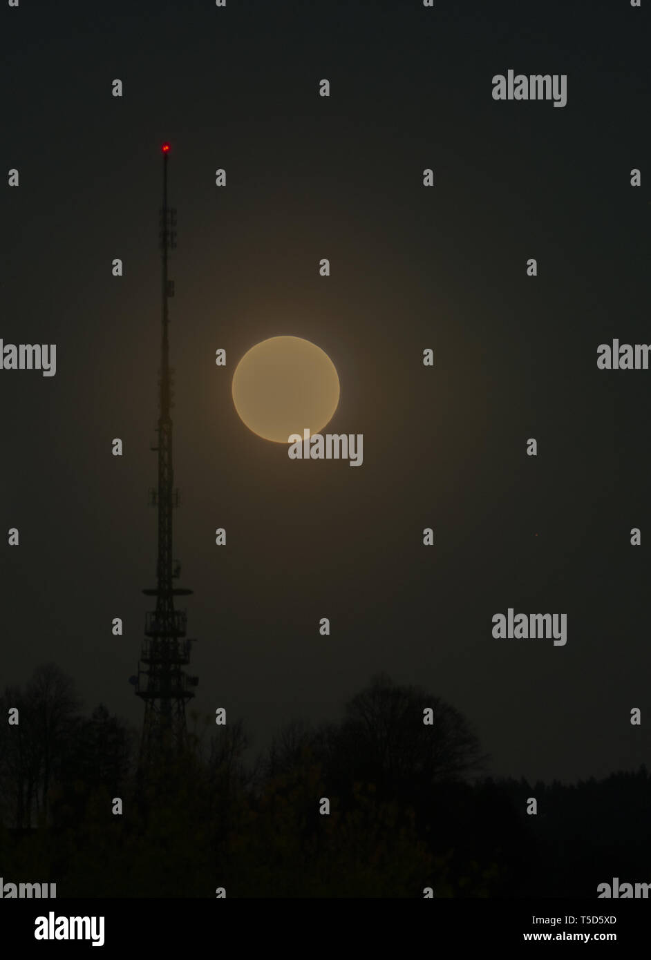 A full moon rising into the night sky with a radio antenna and ...