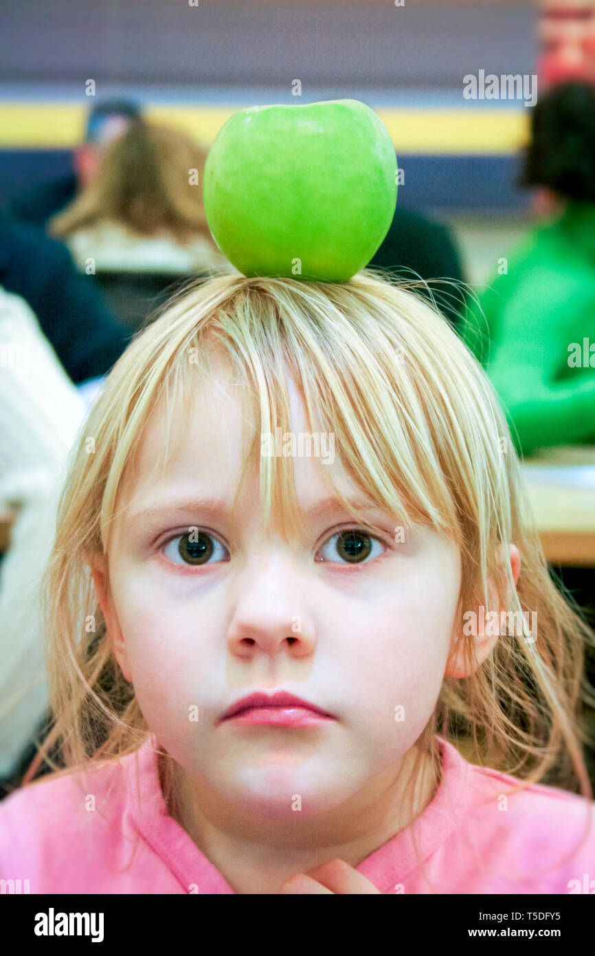Concept image of a cute six-year old girl balancing a green apple on ...