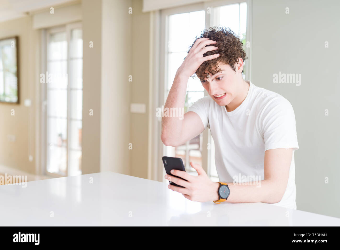 Young man using smartphone at home stressed with hand on head, shocked ...