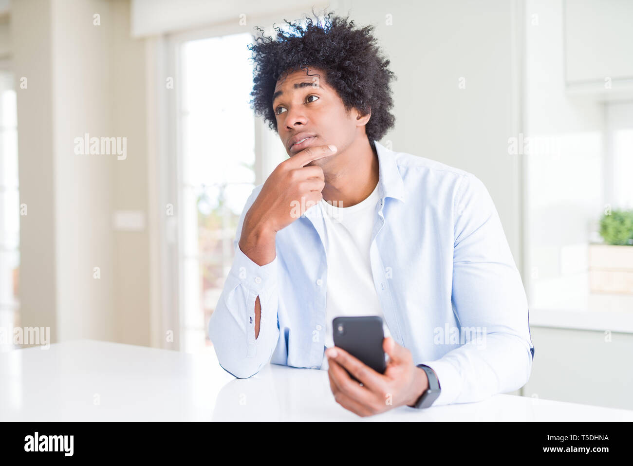 African American man using smartphone serious face thinking about ...