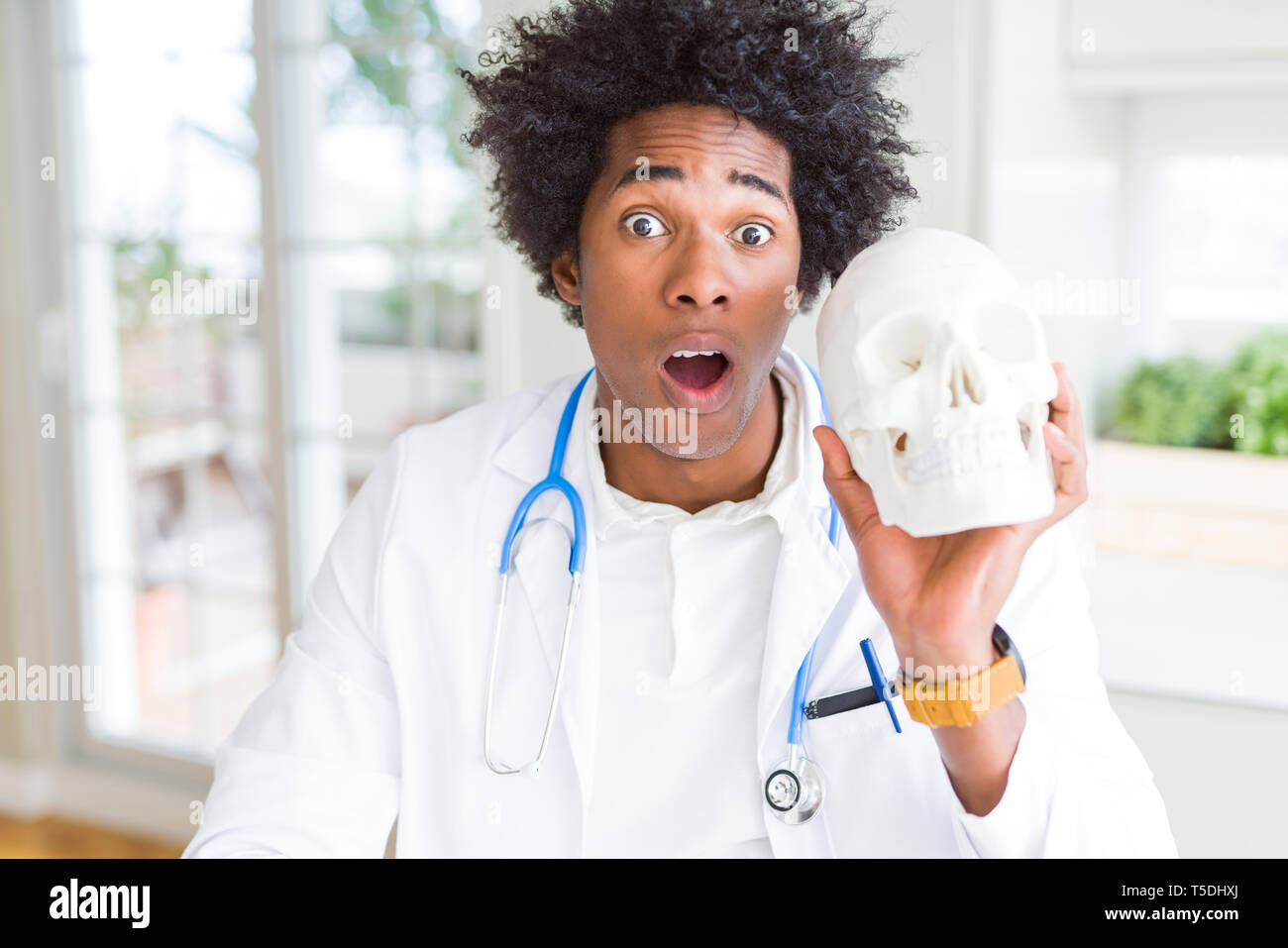 African American doctor man holding skull scared in shock with a ...