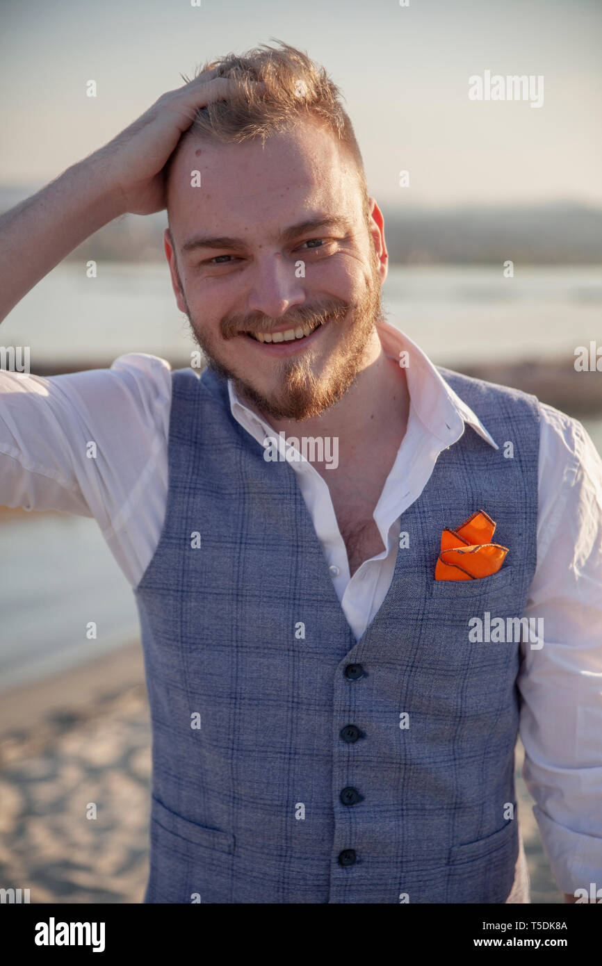 one young man, looking to camera, outdoors carefree posing on a beach ...