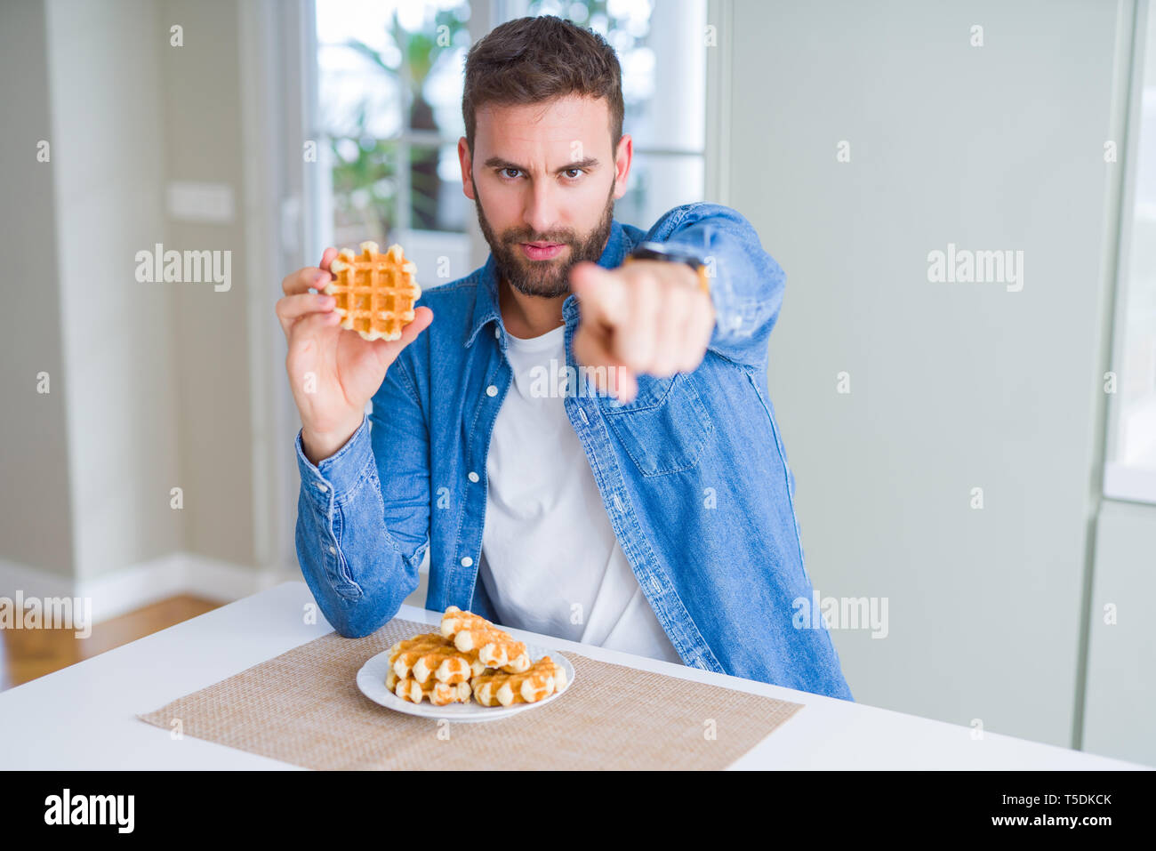 Handsome man eating sweet Belgian pancakes pointing with finger to the ...