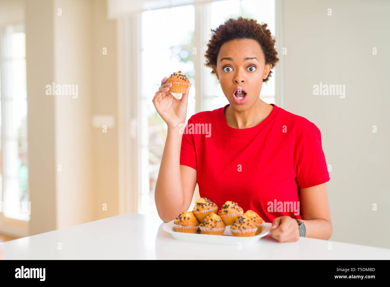 Young african american woman eating chocolate chips muffins scared in ...