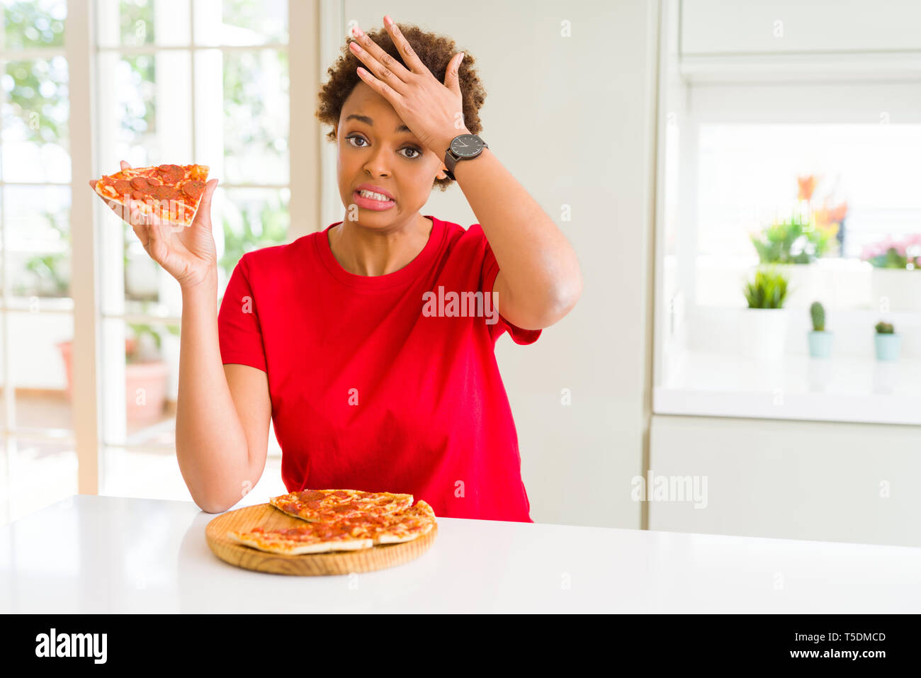 Young african american woman eating tasty peperoni pizza stressed with ...