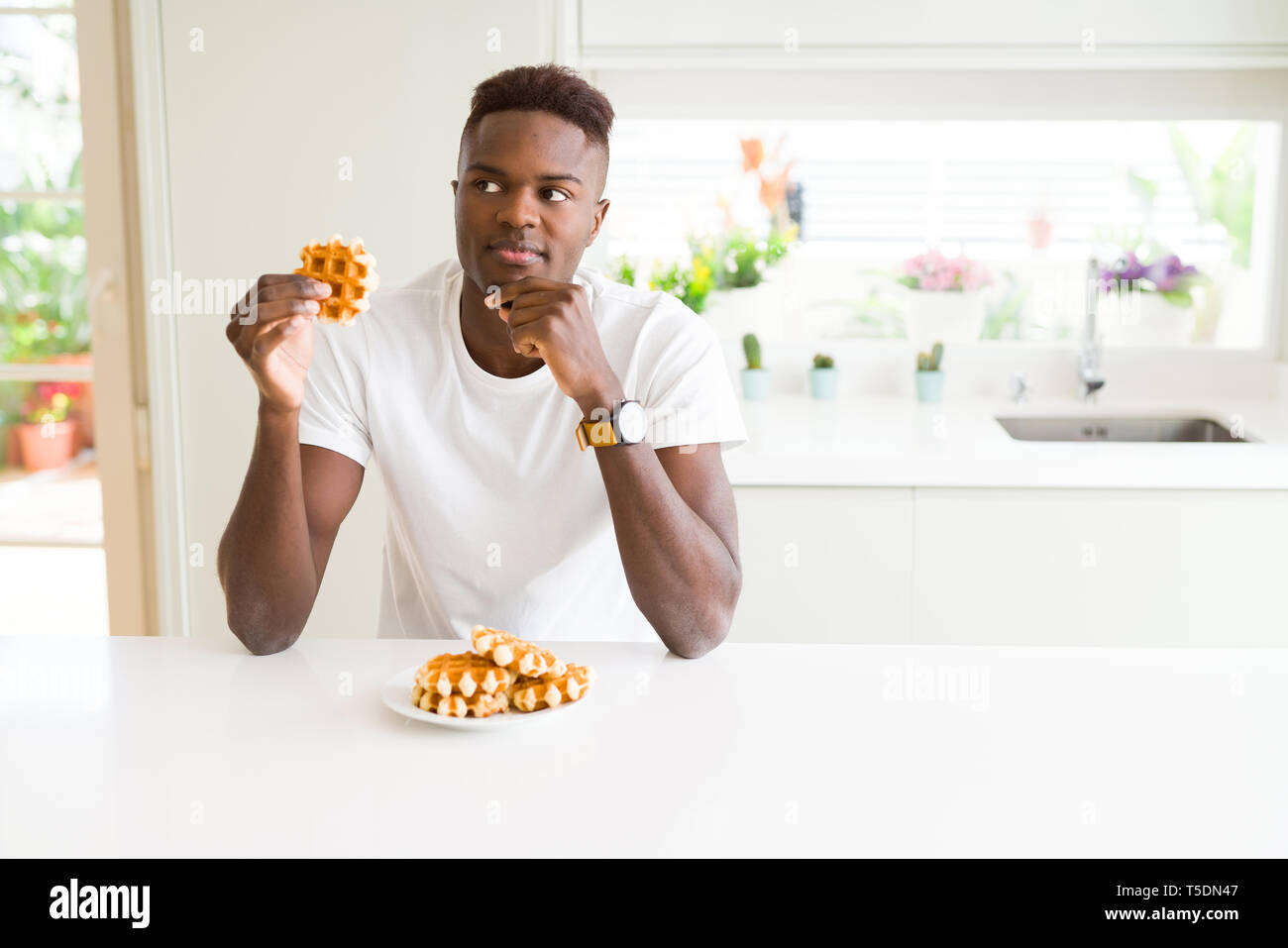 African american man eating sweet Belgian waffle serious face thinking ...