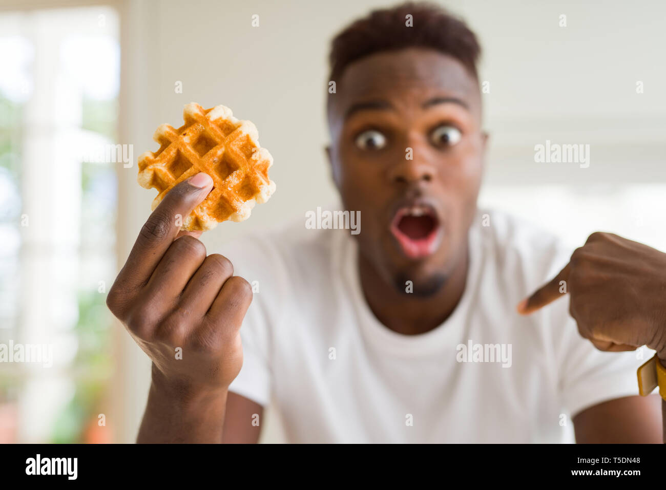 African american man eating sweet Belgian waffle with surprise face ...