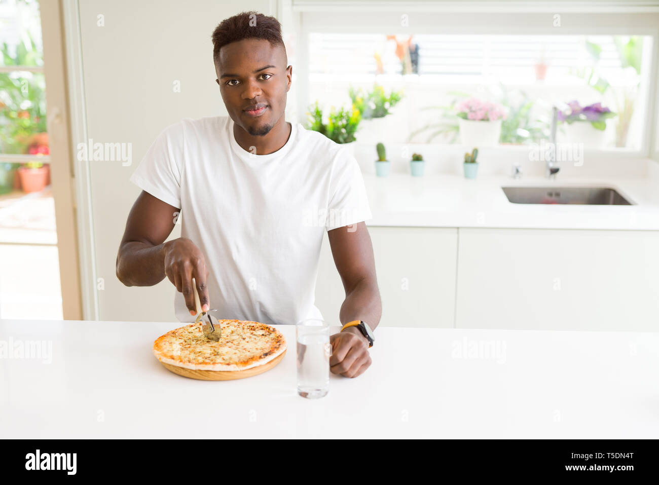 African american man eating cheese pizza at home with a confident ...