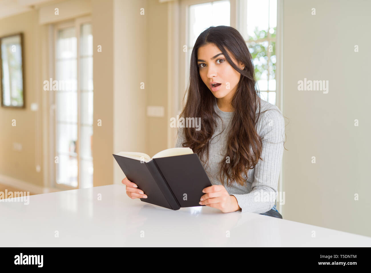Young woman reading a book scared in shock with a surprise face, afraid ...