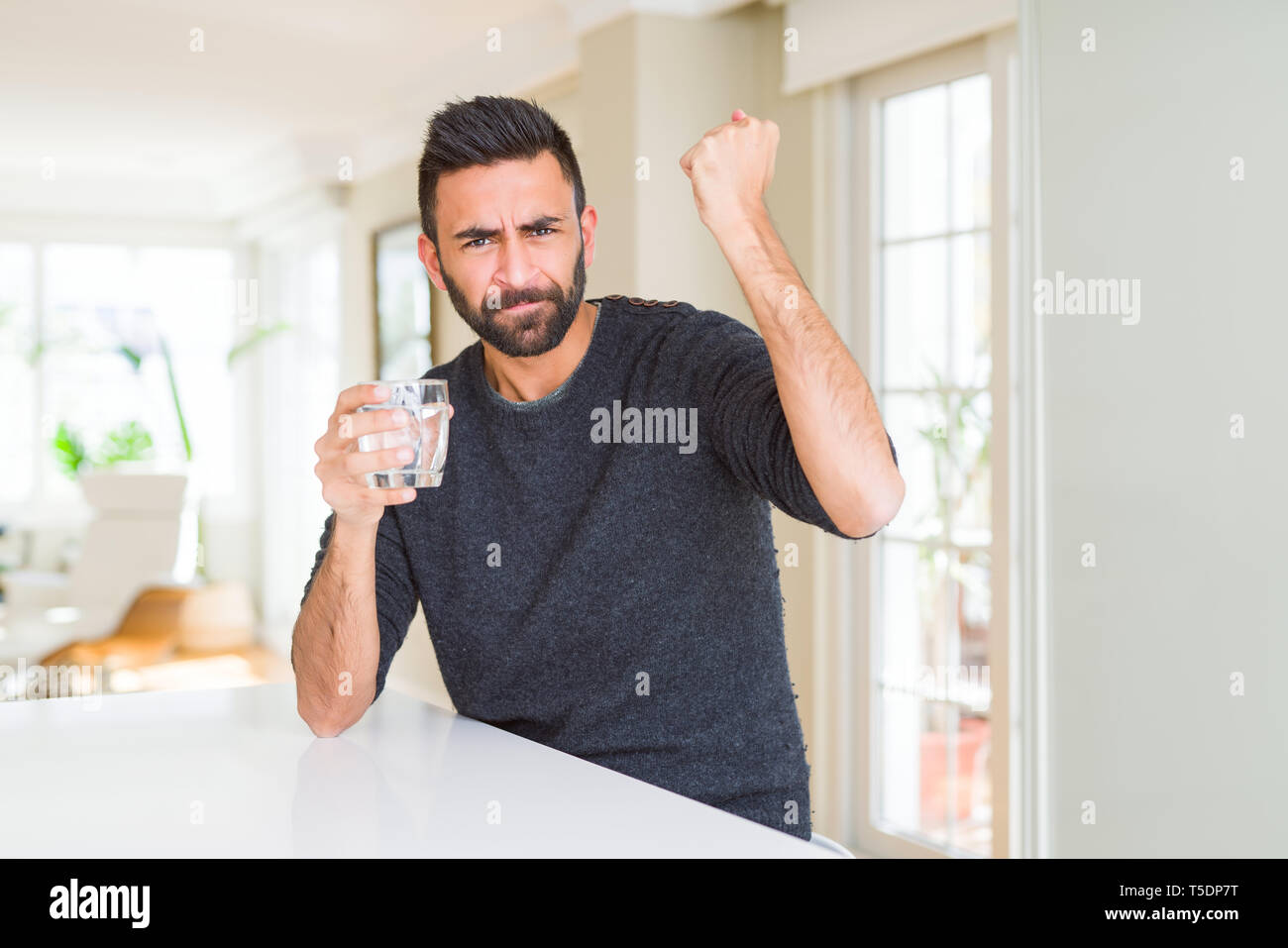 Handsome hispanic man drinking a fresh glass of water annoyed and ...